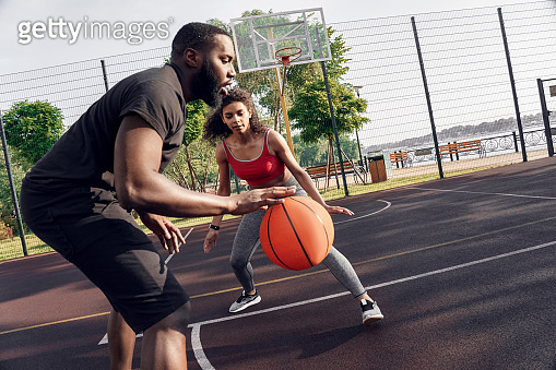 Outdoors Activity. African couple on basketball court guy dribbling ...