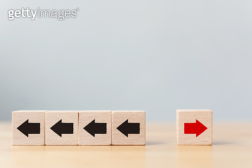 Hand holding wooden block with red arrow facing the opposite direction ...