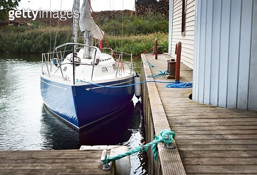 Blue sloop rigged yacht moored to a wooden pier in a small village ...
