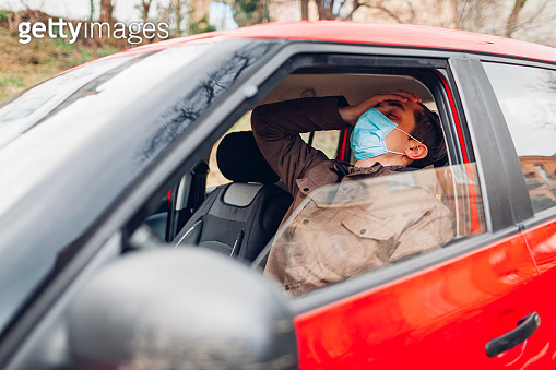 Ill man sitting in car wearing protective mask feels fever sick has flu ...