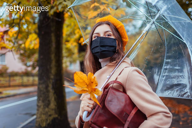 Stylish woman in protective mask walks on autumn city street under ...