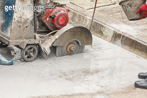 Worker using diamond saw blade machine cutting concrete road at ...