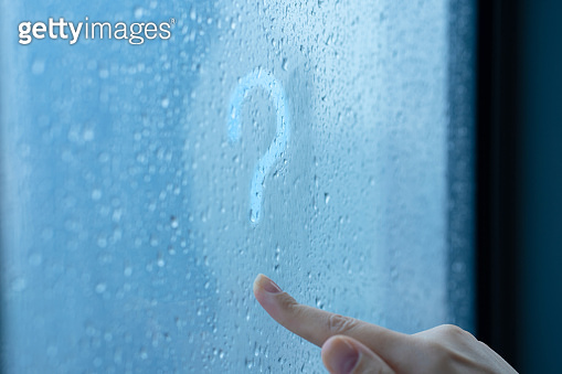 Female hand draws a question mark on a foggy window during the rain. A ...