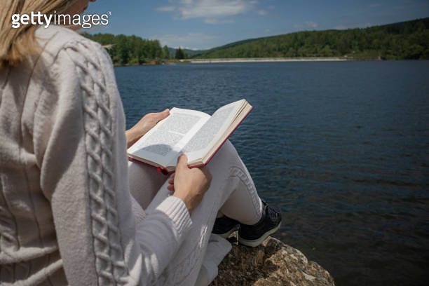 Woman with book on legs lap reading near lake in nature. Relaxation and ...