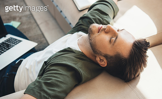 Upper view photo of a tired man lying near the sofa on the floor with a ...