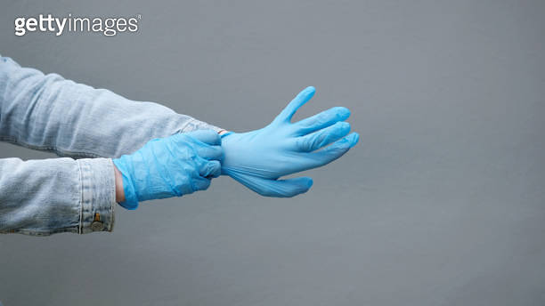 A girl in a denim jacket puts on her hands blue medical gloves against ...