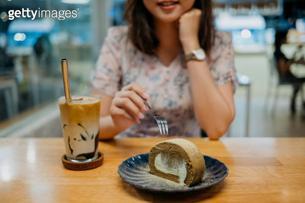 Happy young asian woman enjoying Swiss roll and coffee in cafe ...