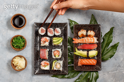 Close up of hand taking roll with chopsticks from a plate (1278978937 ...