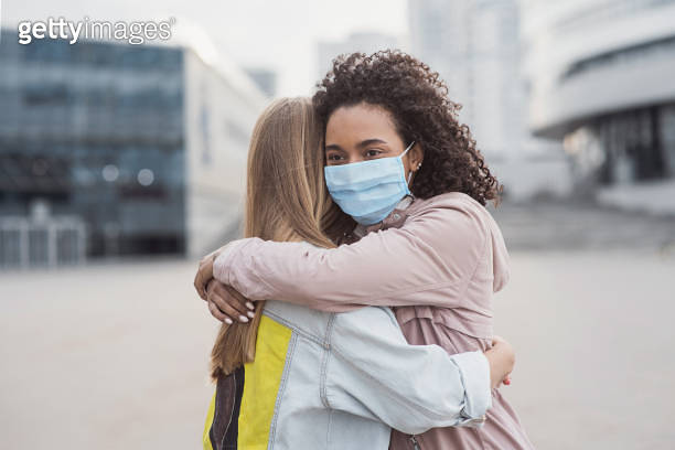 Meeting of two happy friends hugging in the street wearing protective ...