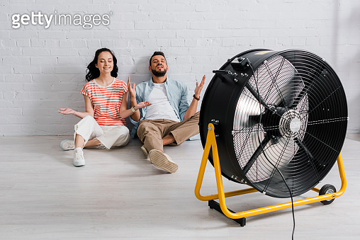 Happy couple sitting on floor near electric fan at home 이미지 (1254115384 ...
