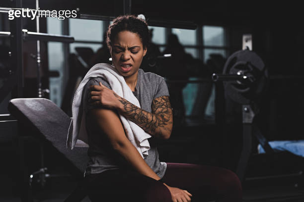 injured african american woman with tattoo touching hand while ...
