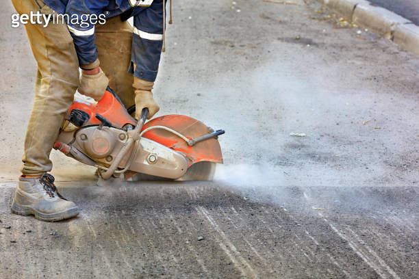 A construction worker using a portable gasoline saw cuts asphalt to ...