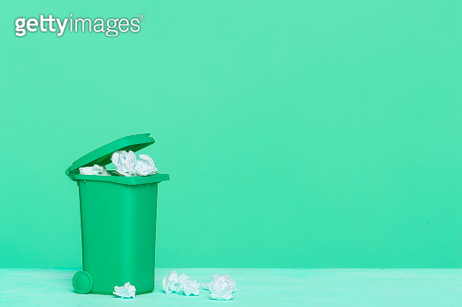A green plastic garbage bin and paper on green background, great for ...
