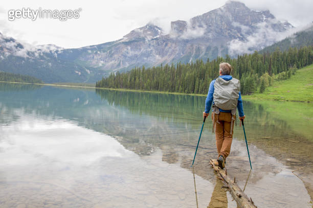 Hiker balances along log floating in alpine lake 이미지 (1264333025) - 게티이미지뱅크