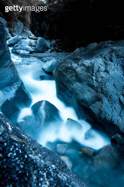 High mountain stream flows over green rocks in rugged environment 이미지 ...