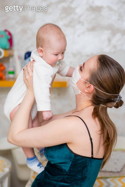 Mother in medical protective mask holds her baby in her arms during the ...