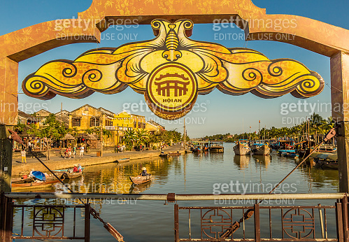 The bridge and town sign in Hoi An, Vietnam, with the town and boats in ...