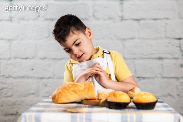 a boy dressed as a baker laughs happily at his bakery set with bread ...