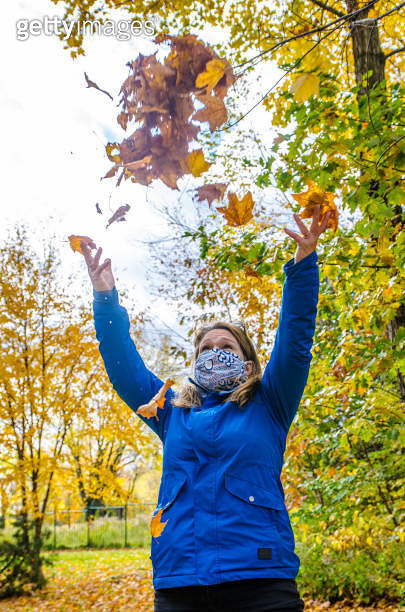 Woman wearing face mask throwing autumn leaves in the air (1280342539 ...