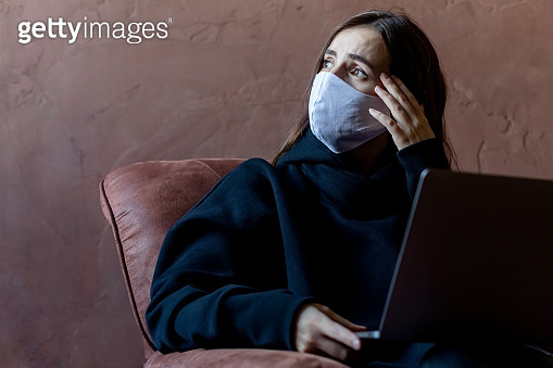 Depressed woman with face mask working on laptop computer at the home ...