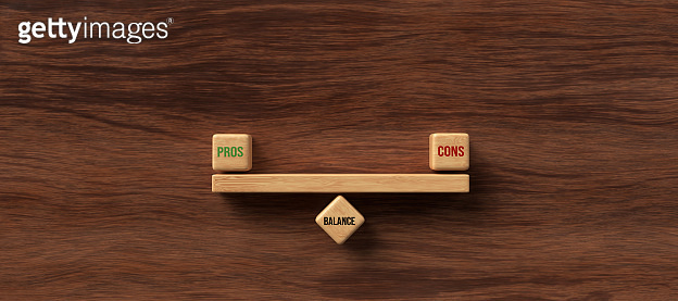 wooden blocks formed as a seesaw with the words PROS, CONS and BALANCE ...