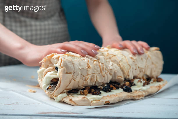 Woman in checkered apron rolls meringue roll on a white vintage wooden ...