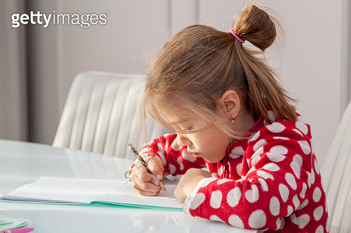 child girl doing homework sitting at kitchen table, learning at home ...