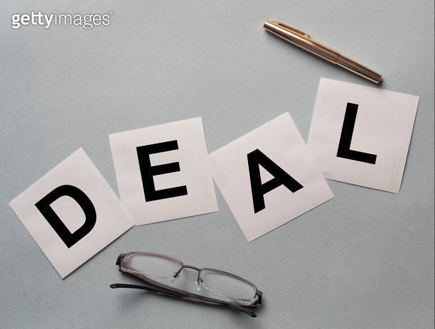 Word DEAL on white stickers and golden pen and glasses on grey blue ...