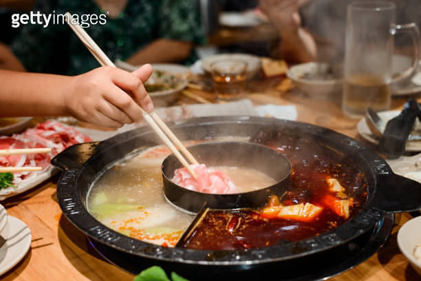 Close view on hot pot. Man dipping meat slices in broth, using ...
