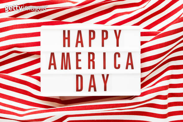 HAPPY AMERICA DAY written in light box on red background. Top view ...