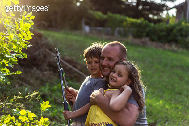 Dad and his two kids with secateurs cutting off leaves in the garden ...