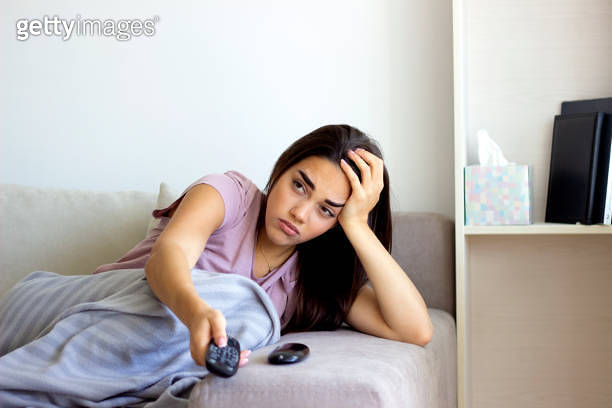 Brunette woman relaxing at home, curled up in a blanket, holding the ...
