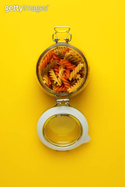 Tricolor fusilli pasta in a glass jar top view on a yellow background ...