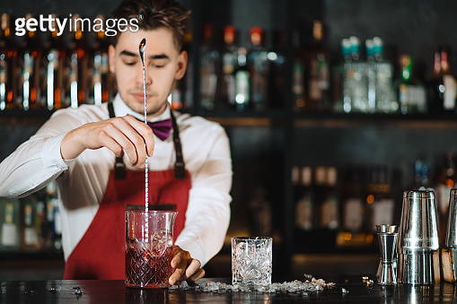 Barman holding a long spoon and glass filled with ice cubes on the bar ...