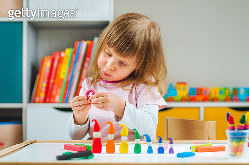 Little girl molding colorful gnomes from child's play clay on the table ...