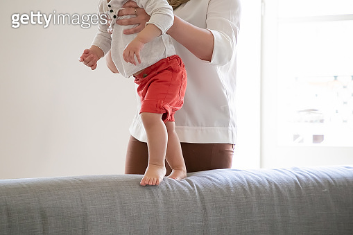 Mother helping baby to walk on couch at home (1287579863) - 게티이미지뱅크