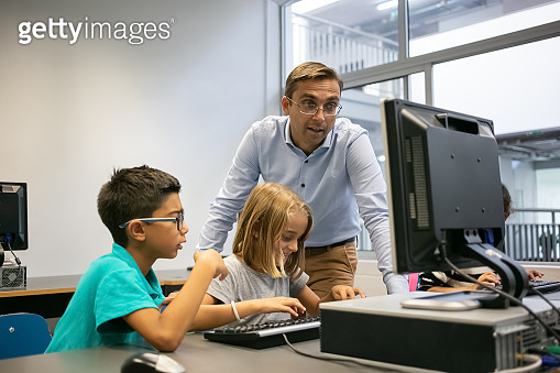 Happy kids sitting in front of computer monitor and learning IT ...