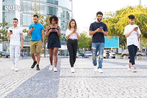 Front view of friends using phones while walking on street (1204162693 ...