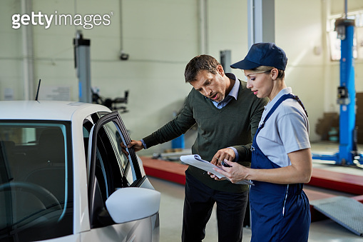 Auto repairwoman and her customer going through paperwork in a workshop ...