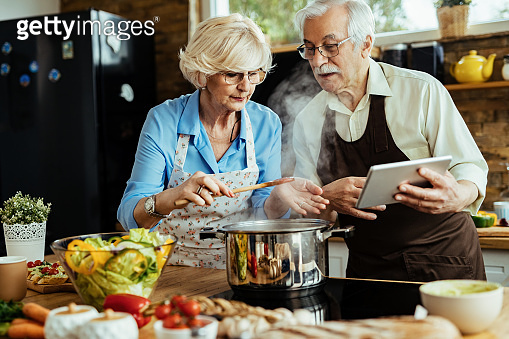 Senior couple cooking while following recipe on touchpad in the kitchen ...