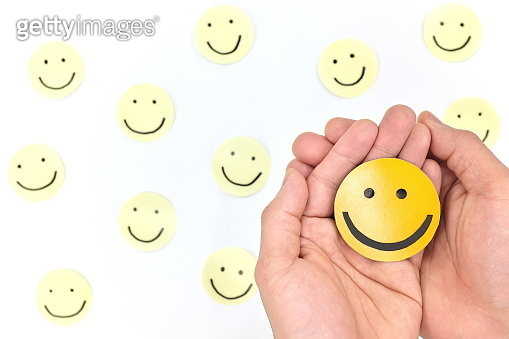 Hand holding a smiling face icon among a group of happy emoticons ...