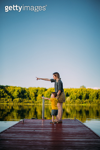 Cool baby boy with mother looking on river standing on pier point a ...