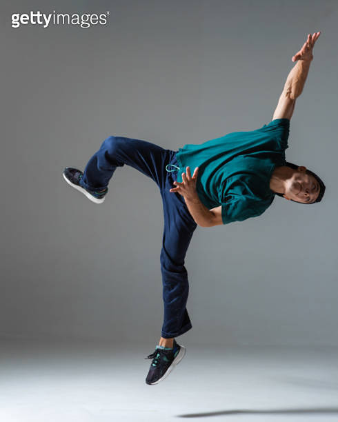 Cool young guy breakdancer jumps dancing hip-hop isolated on gray background. Dance school ...