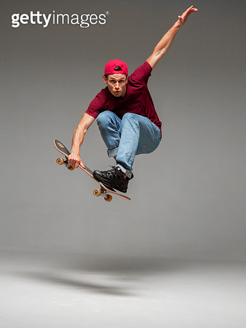 Cool young guy skateboarder jumps on skateboard in studio on gray ...