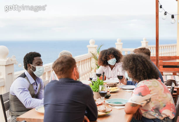 Multiracial people have a dinner outdoor while wearing protective face ...