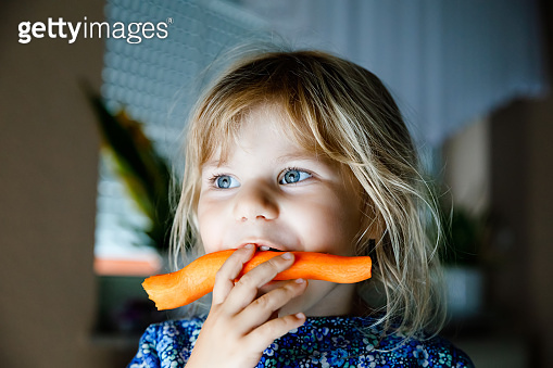 Cute adorable toddler girl holding and biting into fresh carrot ...
