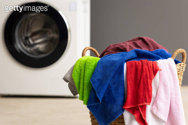 Piles of laundry in the basket and the washing machine are placed close ...