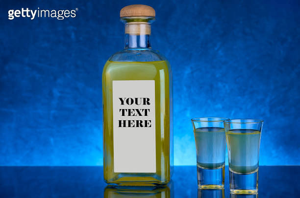 YELLOW LIQUOR BOTTLE AND SHOTS, WITH BLUE BACKGROUND AND LABEL WITH ...