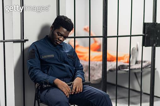 A strong black prison guard guards the cells with prisoners in the ...