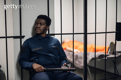 A prison warden guards cells with prisoners sentenced to life in orange ...